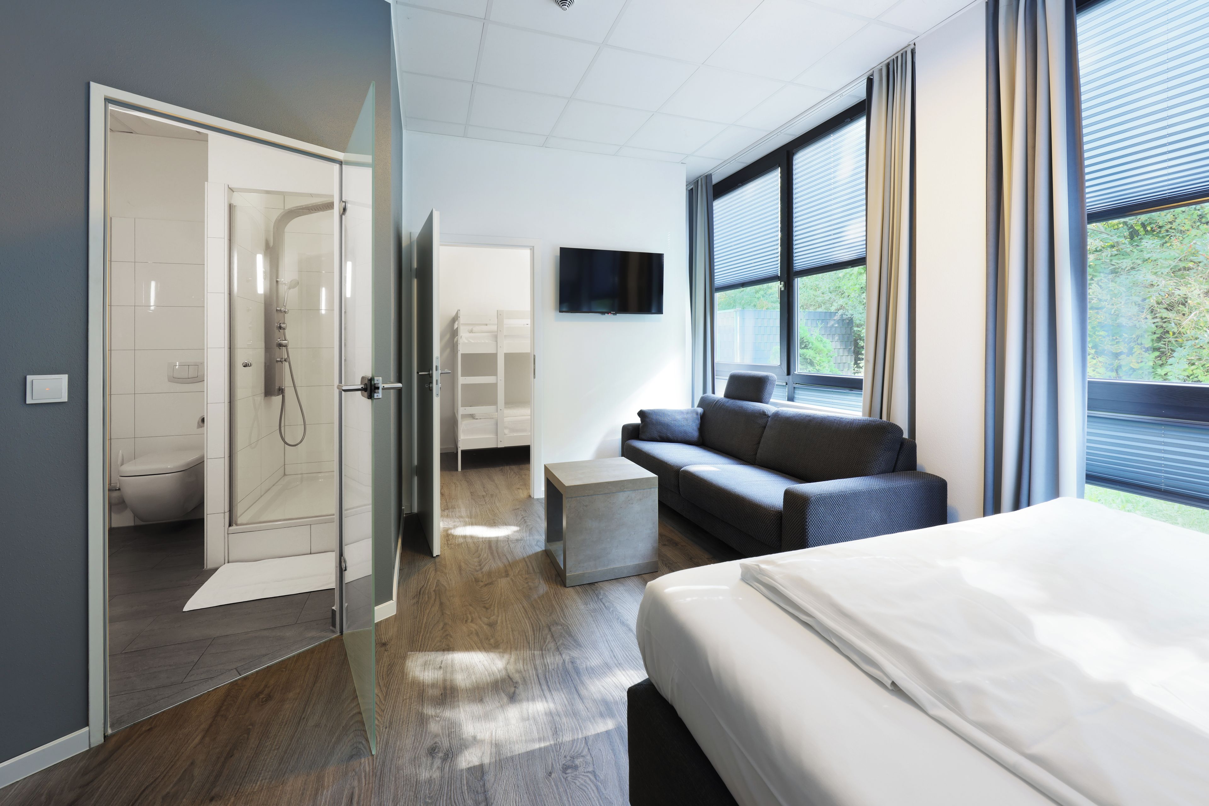 Quarto de hotel moderno com chuveiro, cama, área de estar e televisão.