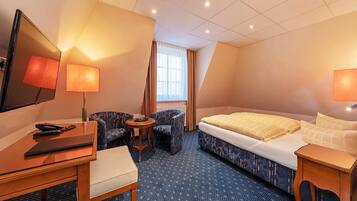 Quarto de hotel com cama, escrivaninha, cadeira, televisão e janela com cortinas.