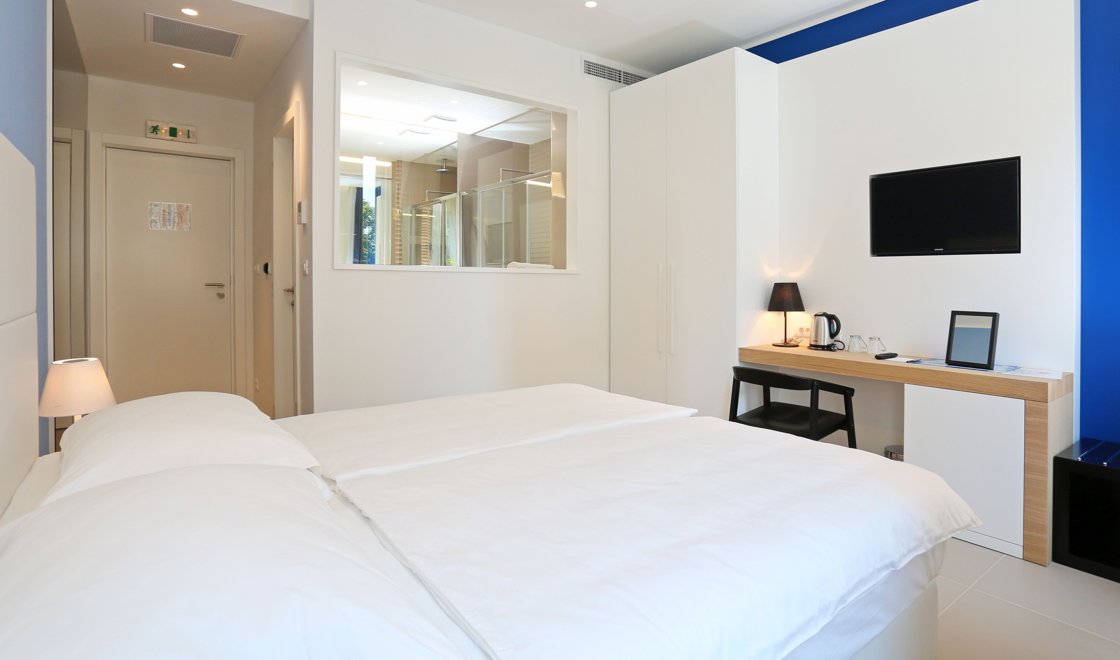 Quarto de hotel com uma cama, uma mesa com abajur, uma televisão e um espelho.