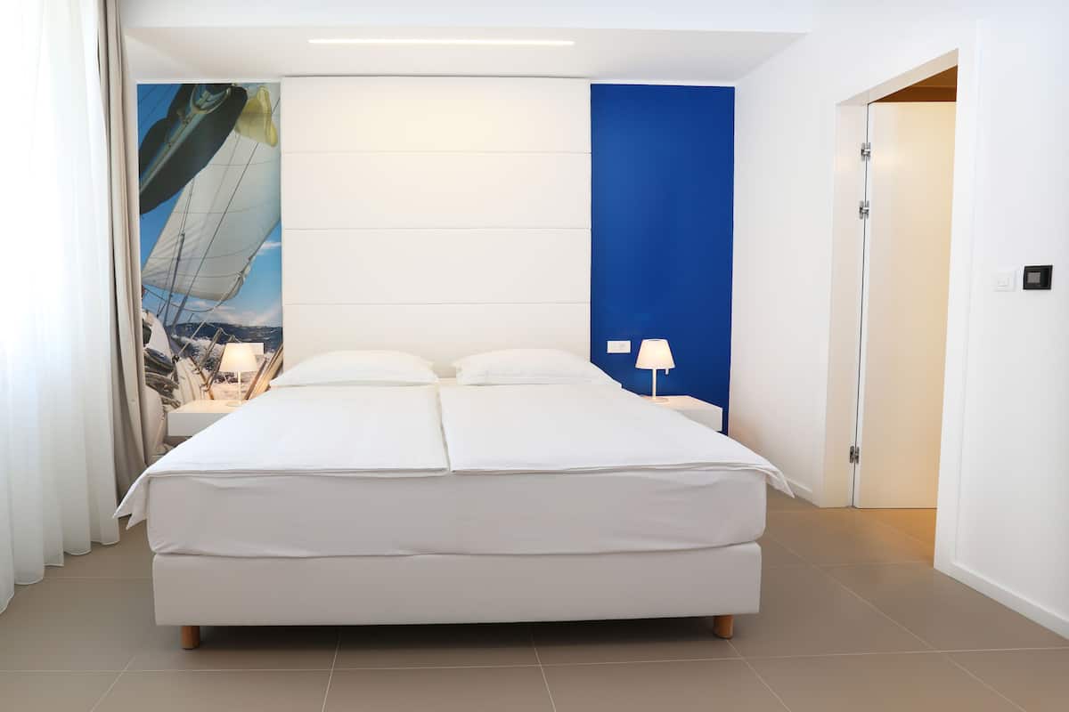 Quarto de hotel moderno com uma cama grande, uma mesa de cabeceira, uma luminária na parede e um mural de um veleiro.