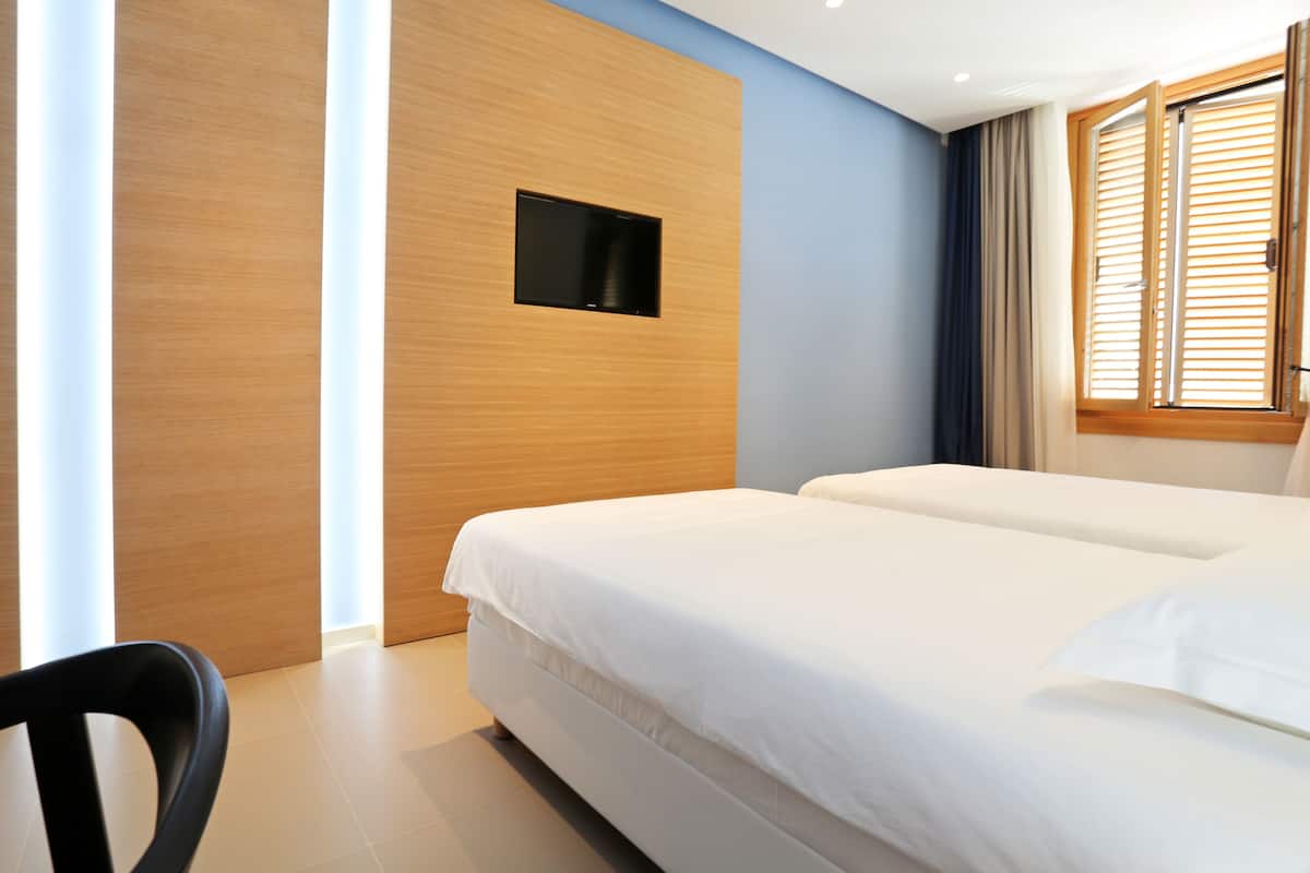 Quarto de hotel moderno com uma cama grande, televisão de tela plana na parede e uma janela com persianas.