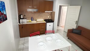 Um espaço de estar compacto com cozinha compacta, sala de jantar com mesa branca e cadeiras vermelhas, e um sofá.