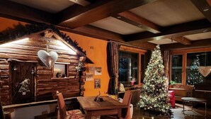 Interior acolhedor de uma cabana de madeira, com uma mesa de jantar de madeira, cadeiras e um pinheiro decorado para o Natal.