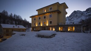 Hotel de vários andares com um pátio coberto de neve, fachada de pedra e vista para as montanhas.