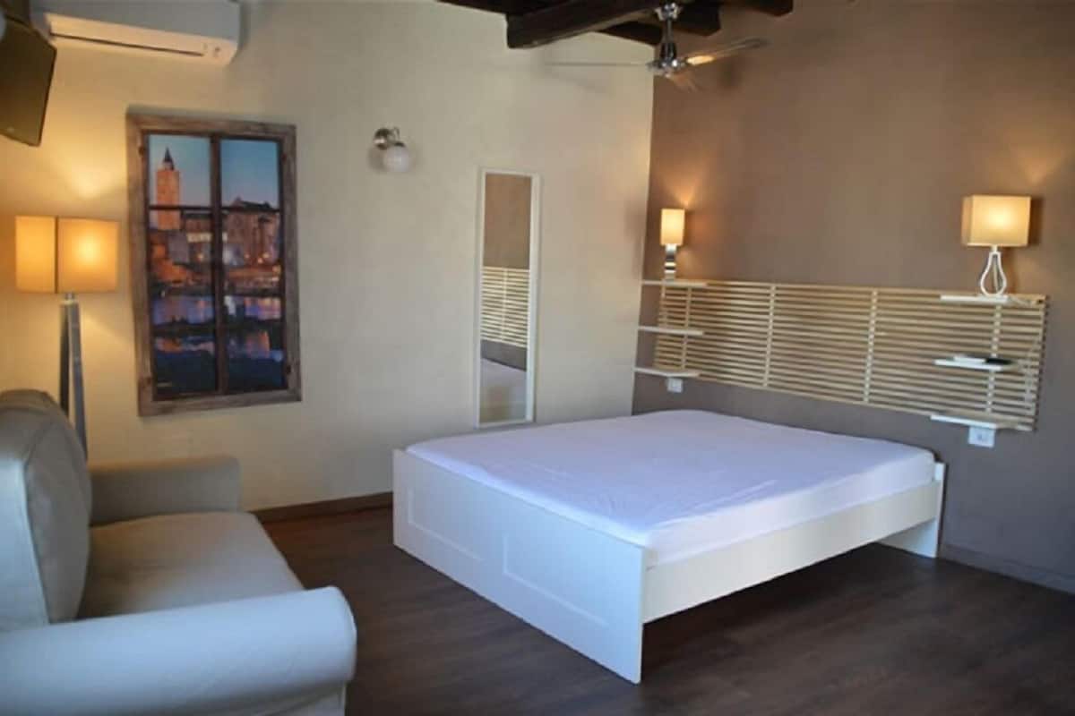 Quarto moderno com cama, poltrona, mesa de cabeceira e luminária fixada na parede.