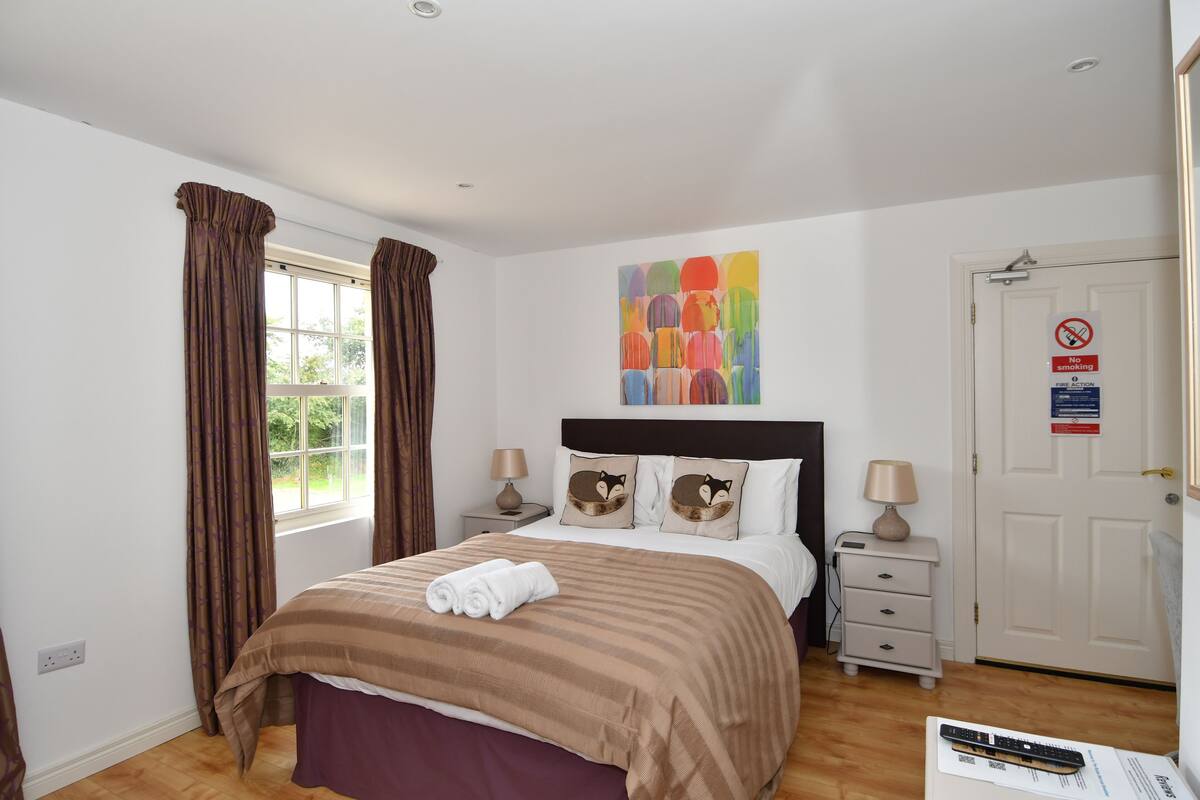 Cama bem arrumada com manta listrada, duas luminárias de cabeceira e um quadro acima da cama.