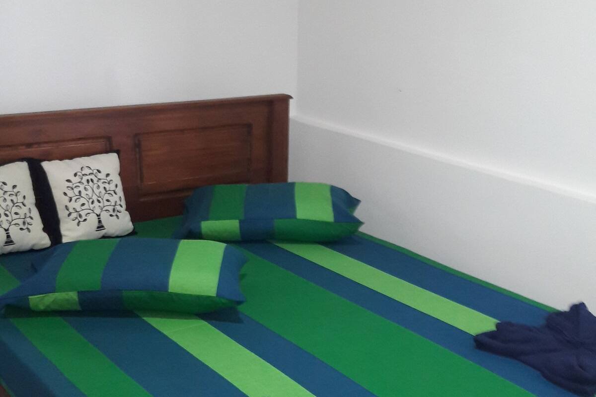 Cama com estrutura de madeira, roupa de cama listrada em verde e azul e almofadas decorativas.