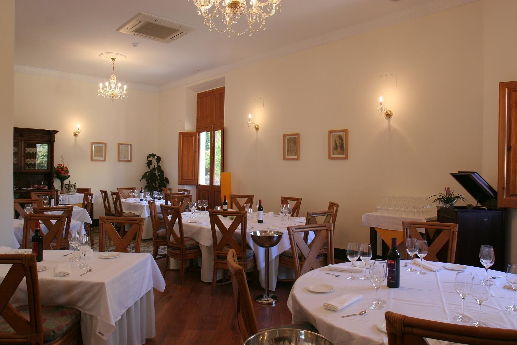 Uma sala de jantar com mesas redondas, cadeiras de madeira e lustres.