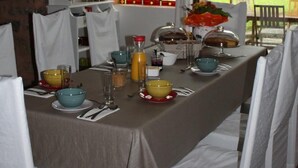 Uma sala de jantar com uma mesa posta para quatro, cadeiras brancas e vista para um jardim pela janela.
