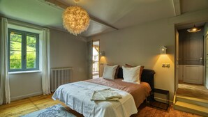 Quarto com cama grande, janela com cortinas, radiador e luminária pendente.