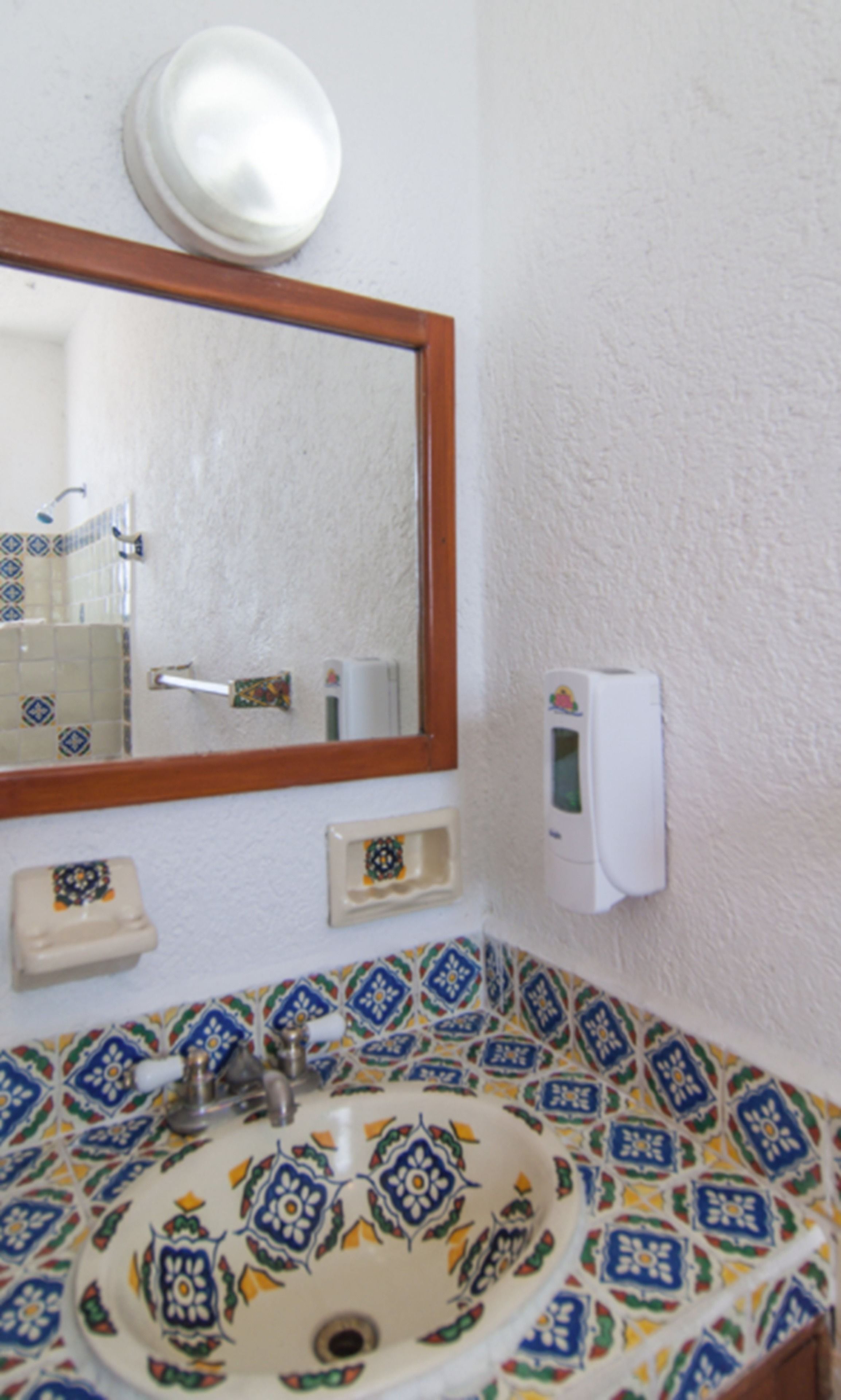 Casa de banho com uma pia branca, espelho e dispensador de sabonete.