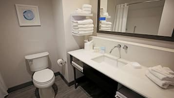 Uma casa de banho moderna com sanita branca, lavatório com espelho e um porta-toalhas com toalhas dobradas.