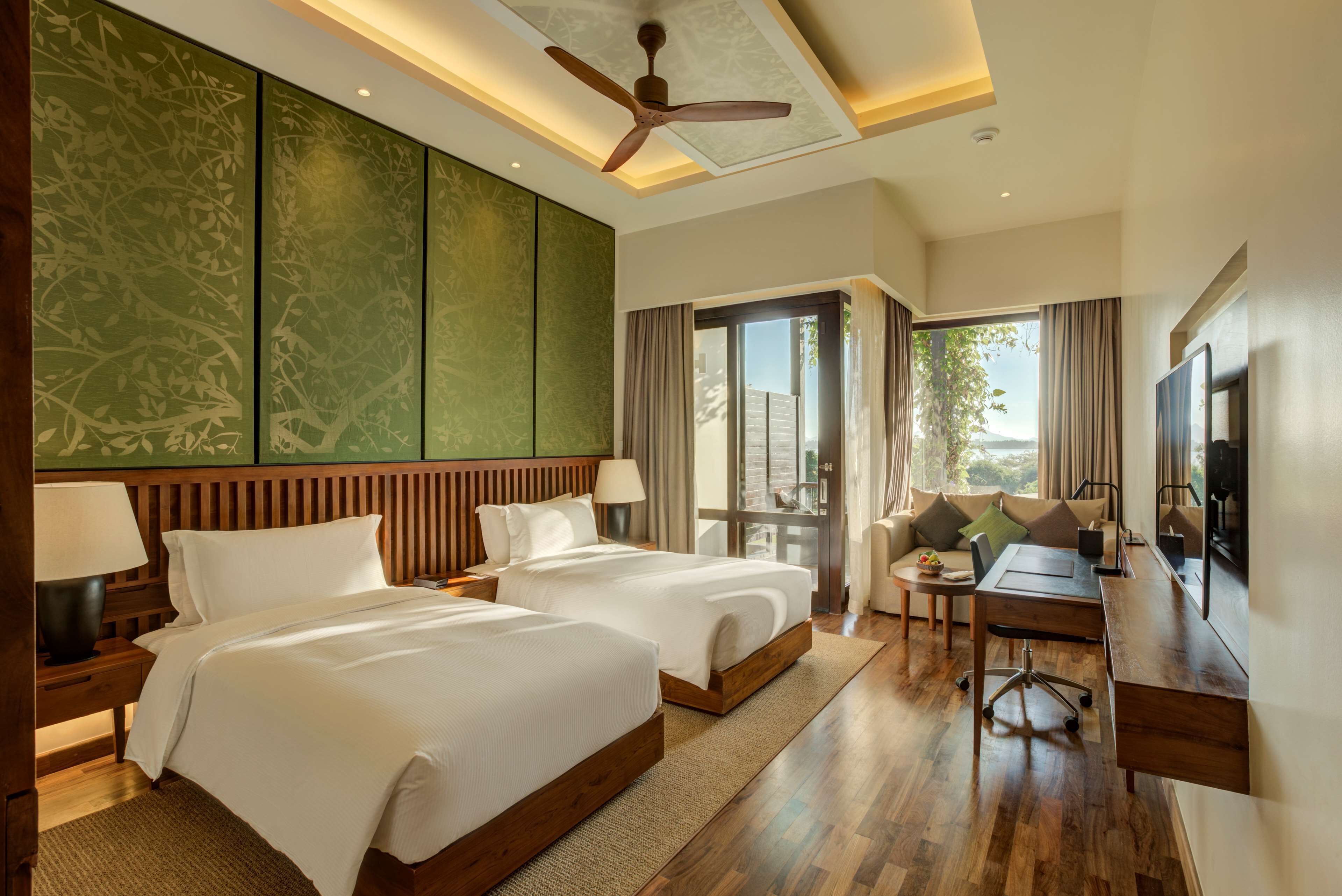 Quarto de hotel com duas camas, uma escrivaninha, televisão e varanda com vista.