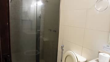 Casa de banho com sanita, cabine de duche, lavatório e um contentor de lixo.