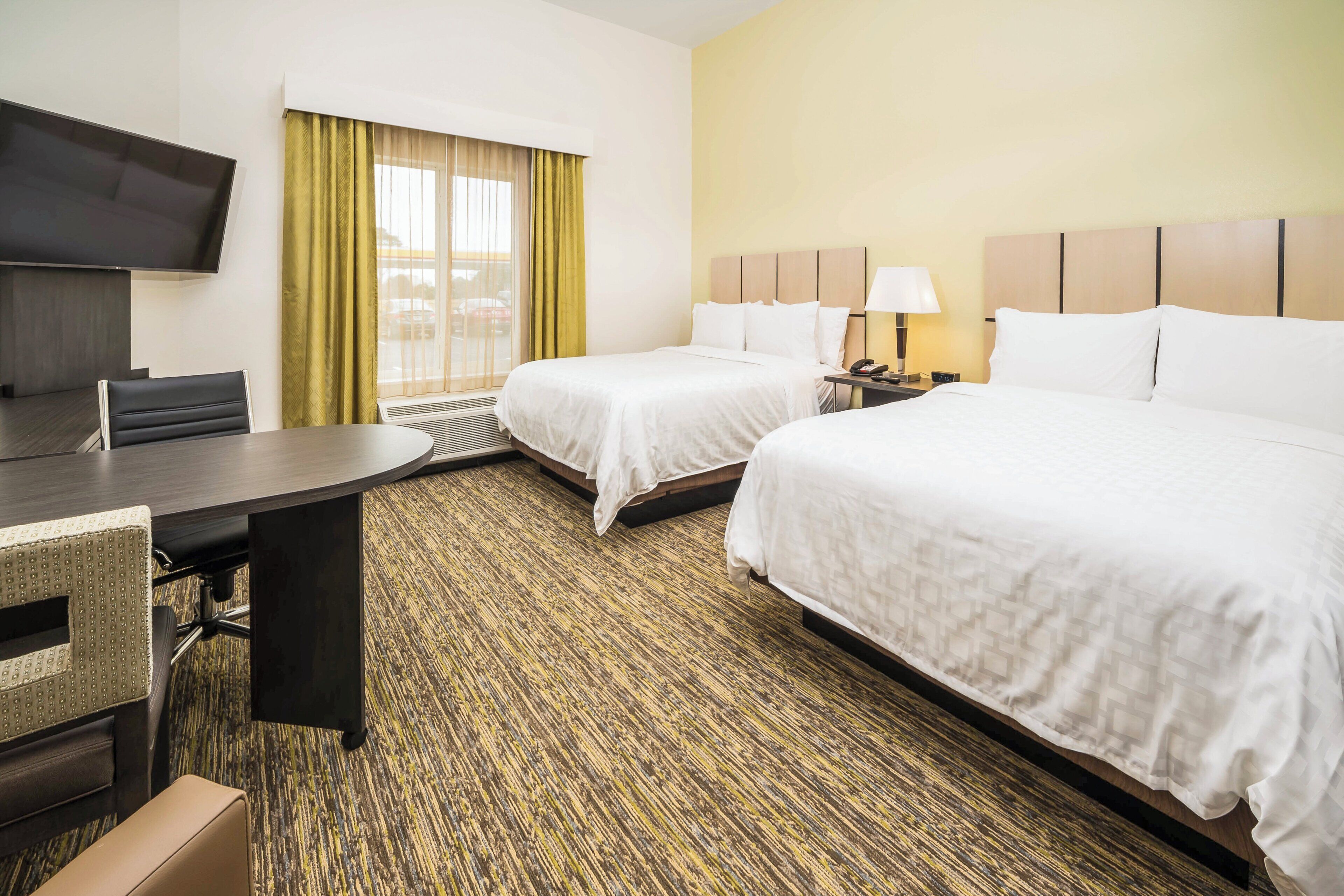 Quarto de hotel com duas camas, uma escrivaninha, uma cadeira, televisão e janela com cortinas.