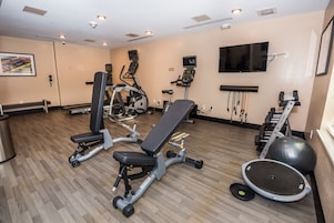 Uma academia com equipamentos de ginástica, uma televisão e uma TV na parede.
