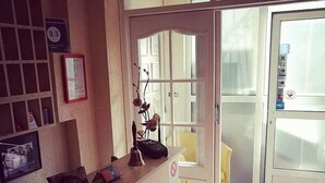 Uma mesa de recepção com uma placa que diz 'RECEPTION', um certificado emoldurado na parede e uma porta que dá para um quarto com carpete vermelho.