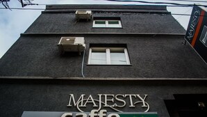 Um edifício com uma placa indicando 'MAJESTY Caffe' e um aparelho de ar condicionado na fachada.