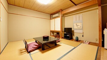 Um quarto japonês tradicional com tatames, uma mesa baixa, uma televisão e uma porta de correr.