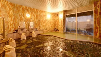 Um onsen japonês tradicional com chão de pedra, paredes de madeira e vista para o exterior.