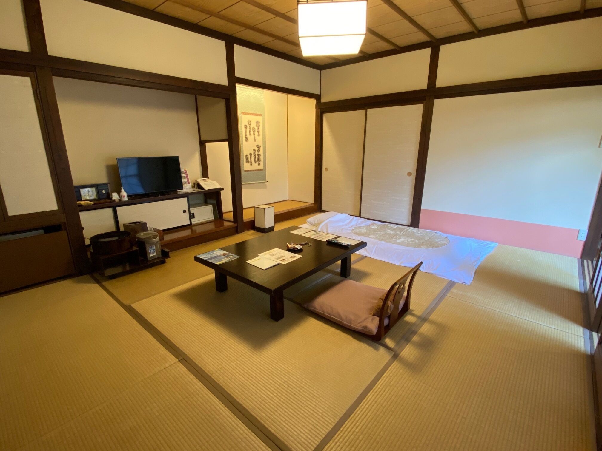 Um quarto japonês tradicional com tatames, uma mesa baixa com almofadas, uma televisão e uma porta de correr.