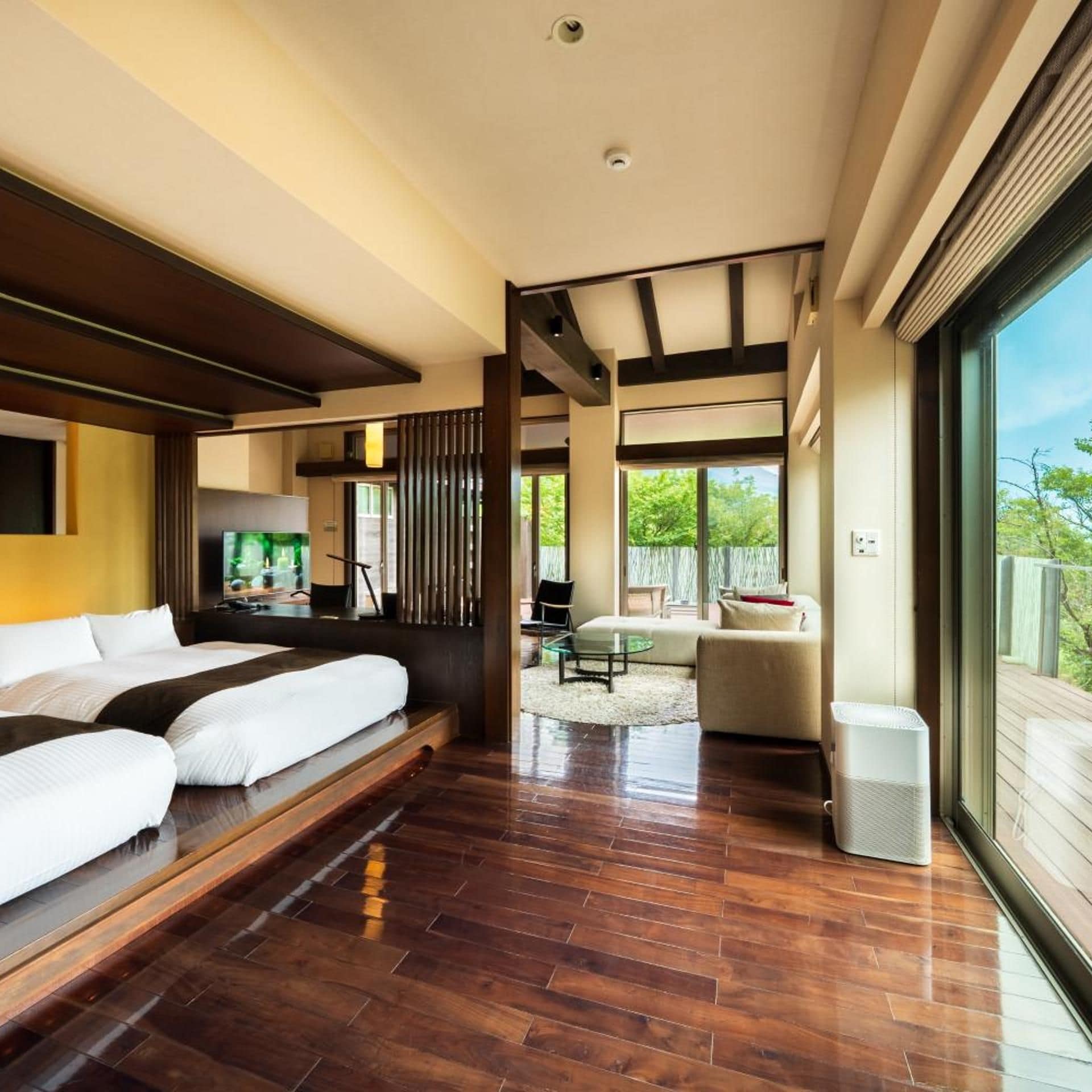 Quarto de hotel moderno com uma cama grande, um espaço de estar e vista para o exterior.