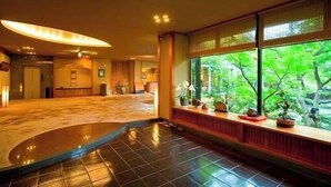 Um hall de hotel com um balcão de recepção curvo, uma janela grande com vista para áreas verdes e um chão de azulejos.