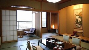 Um quarto japonês tradicional com tatames, uma mesa baixa, assentos e uma janela grande.