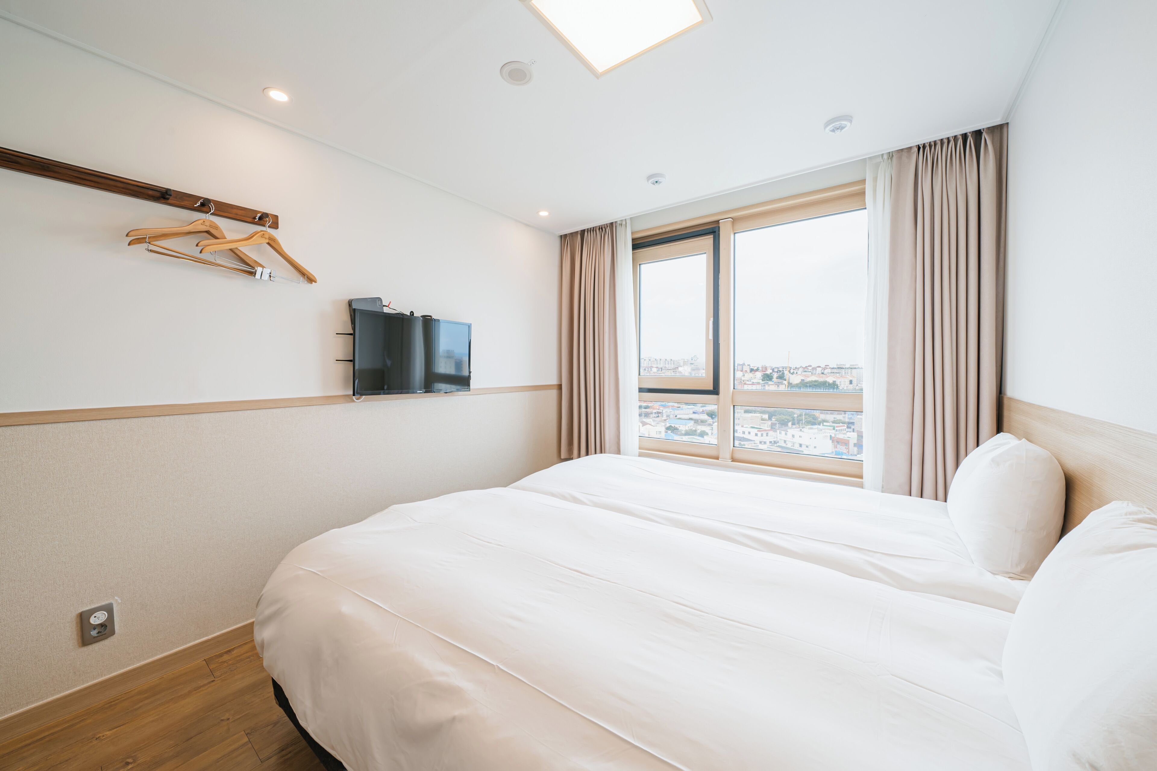 Quarto de hotel com uma cama grande, televisão, janela com cortinas e vista para a cidade.