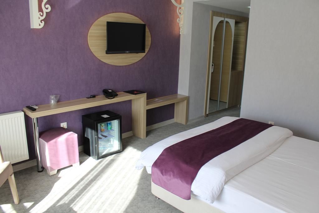 Quarto de hotel com cama, escrivaninha, computador, televisão e minibar.