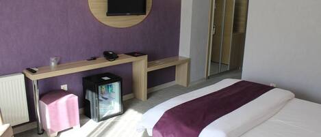 Quarto de hotel com cama, escrivaninha, computador, televisão e minibar.
