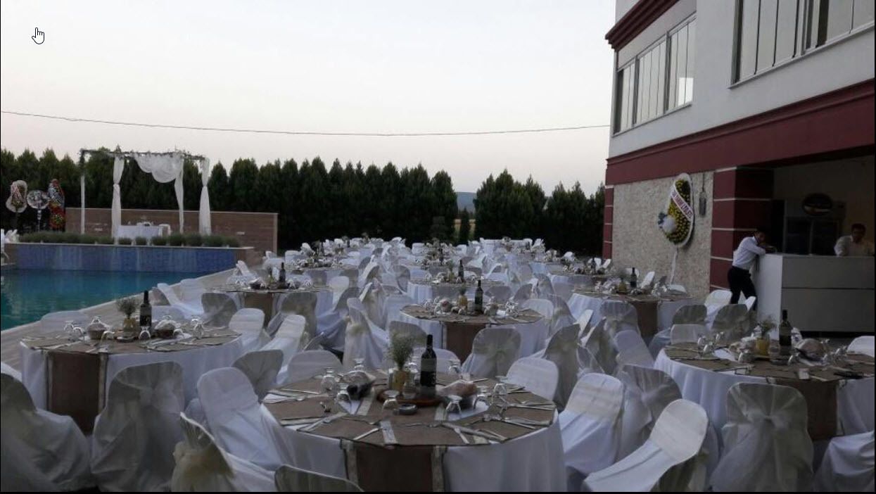 Uma área de banquetes ao ar livre com mesas redondas preparadas para refeições, cercada por capas brancas nas cadeiras.