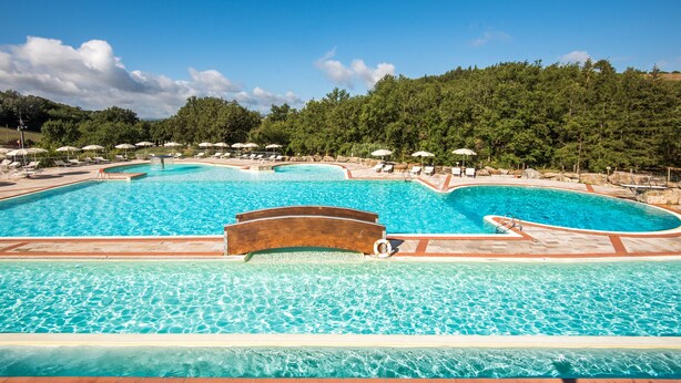 Uma grande piscina ao ar livre com várias áreas e espreguiçadeiras.
