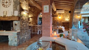 Interior com paredes de pedra, vigas de madeira, lareira e uma área de refeições com mesas e cadeiras.