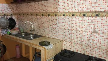 Uma cozinha com revestimento de azulejos, pia, fogão e cilindro de gás.