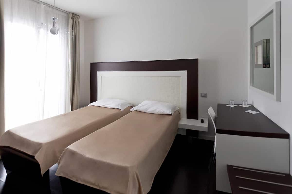 Quarto de hotel com duas camas de solteiro, uma escrivaninha e uma cadeira.
