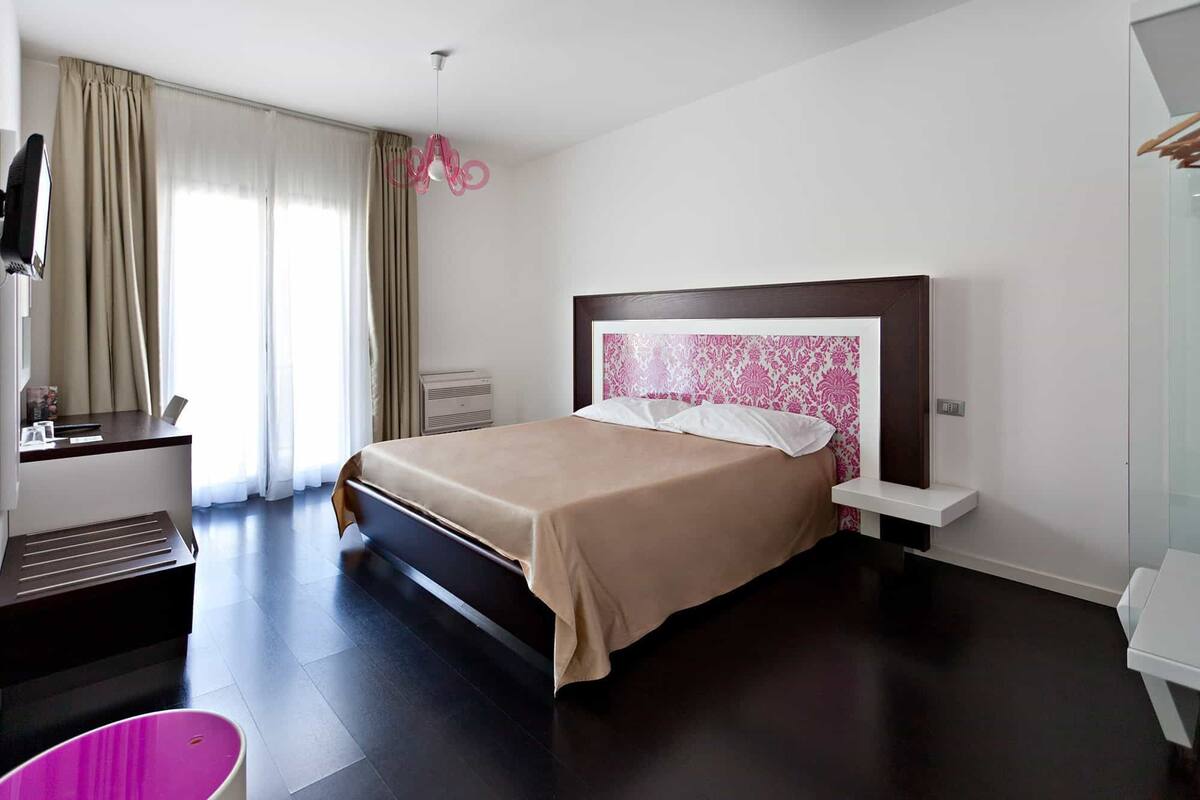 Quarto de hotel moderno com cama, mesa de cabeceira e escrivaninha com cadeira.