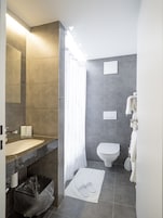 Uma casa de banho moderna com bancada de granito, lavatório branco, sanita e cortina de chuveiro.