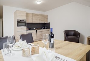 Uma área de refeições com mesa de madeira posta para dois, uma garrafa de vinho e uma vela.