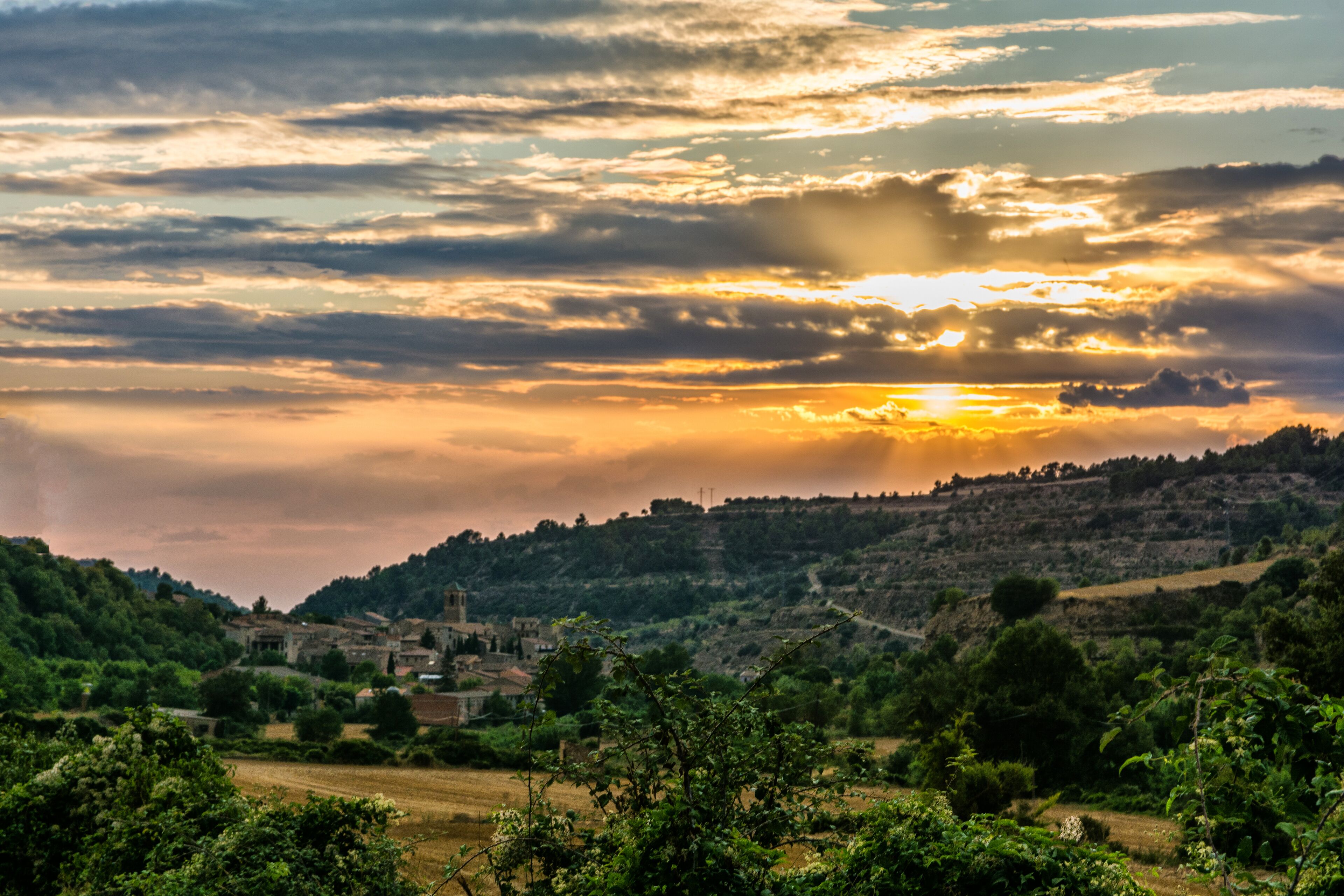 Paisagem rural com uma aldeia situada no vale, rodeada por colinas e vegetação.