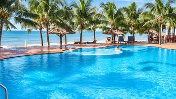 Piscina azul cristalina rodeada por palmeiras e espreguiçadeiras, com vista para o oceano.