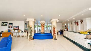 Um hall de hotel com balcão de recepção, assentos azuis e colunas decorativas.