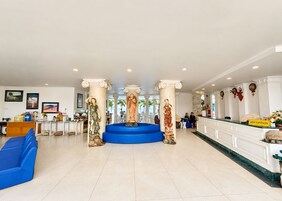 Um hall de hotel com balcão de recepção, assentos azuis e colunas decorativas.