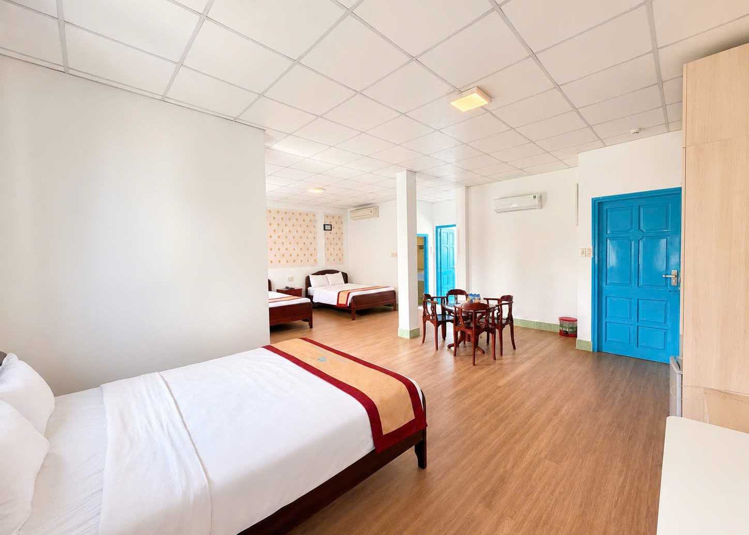 Quarto de hotel com cama, mesa de jantar e cadeiras, e uma porta azul.