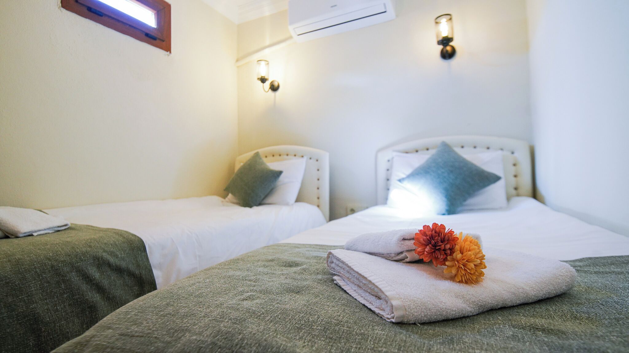 Quarto de hotel com duas camas, janela, ar condicionado e luminárias fixadas na parede.