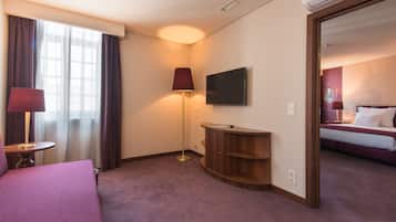 Quarto de hotel com cama, televisão, luminária, escrivaninha e guarda-roupa.