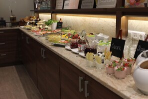 Buffet com diversos alimentos e bebidas, incluindo uma placa com 'Guark' e 'Zabaglione'.