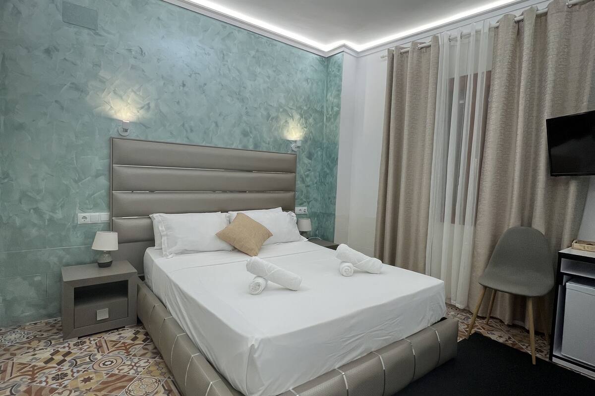 Quarto de hotel moderno com uma cama grande, mesa de cabeceira, televisão e escrivaninha.