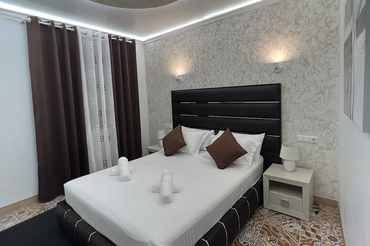 Quarto moderno com uma cama grande, cabeceira, duas mesas de cabeceira e luminária no teto.
