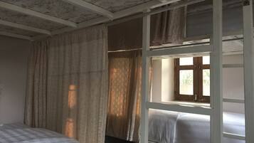 Um quarto com uma cama, uma janela com cortinas e uma beliche.